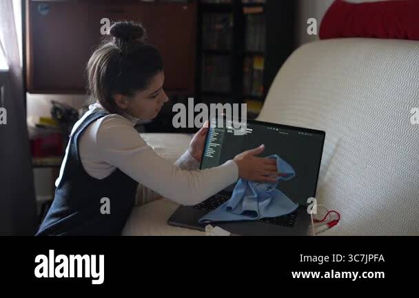 A diligent young woman is thoroughly cleaning her laptop screen with a ...