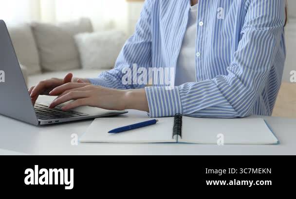 Woman typing on laptop and taking notes at white table indoors, closeup ...