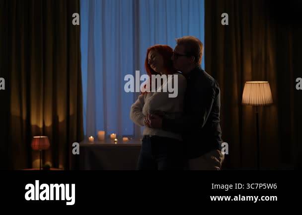 A warmly lit room with a couple embracing and dancing, surrounded by ...