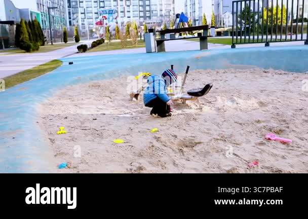 A young child happily plays in a sandbox filled with colorful toys ...