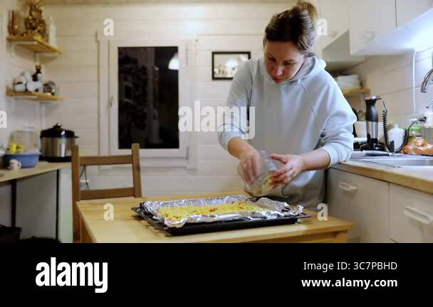 In a warm kitchen, a person carefully sprinkles ingredients over a ...