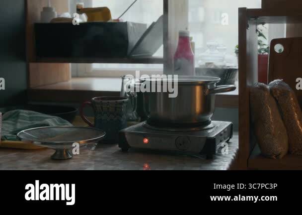 Steam rising from metal pot on red-lit portable stove in cluttered ...
