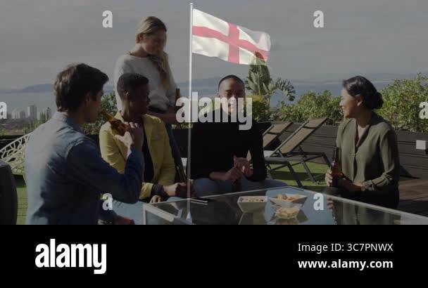 Friends on rooftop with England flag, drinking and snacking ...