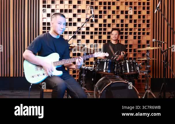 two young asian male musicians playing electric guitar and drums in ...