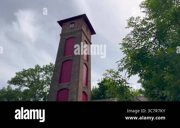 A tall brick tower with red window coverings stands against a partly ...