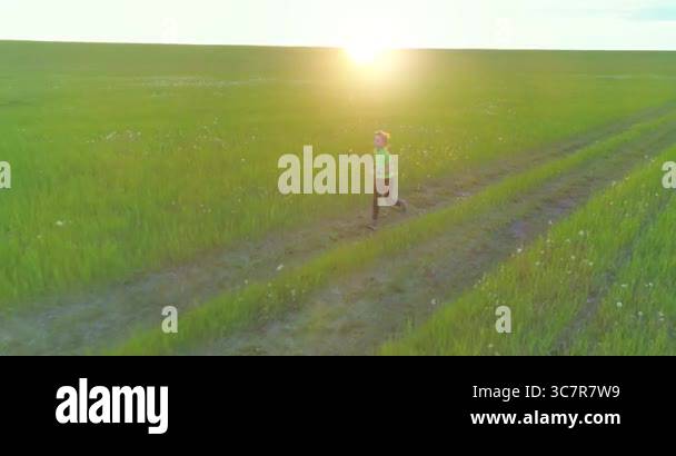 Aerial shoot of a sporty child runs through a wheat field. Evening ...