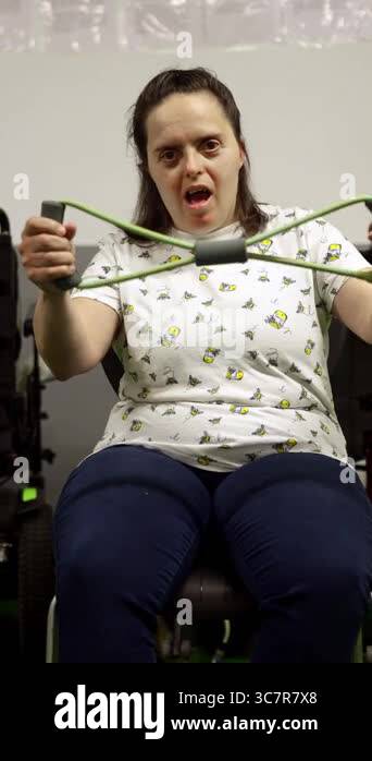 A woman in a wheelchair stretches an exercise cord with focused ...