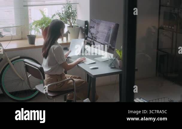Tilt down shot of female programmer coding on computer and throwing paper into recycling bin ...