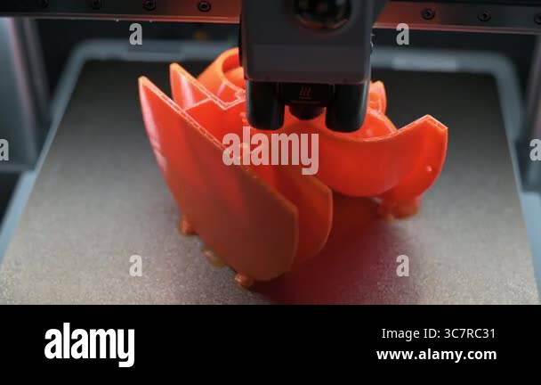 A 3D printer in action, producing a vibrant orange prototype model. The ...