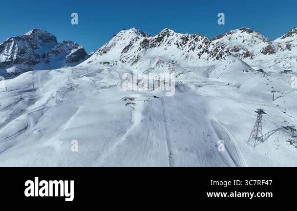 Aerial view over snowy mountain ridge valley with blue sky and cable ...