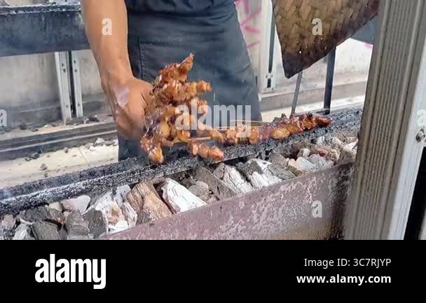 Cinematic shot. The traditonal serving process of lamb satay grilled on ...