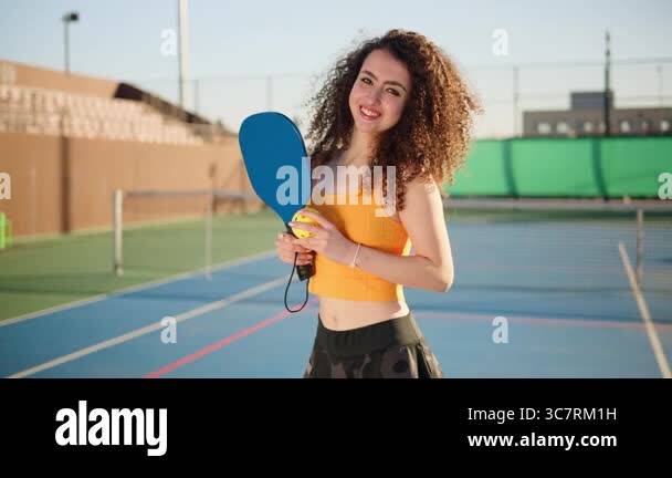 A happy and smiling woman with curly hair holding a Pickleball blue ...