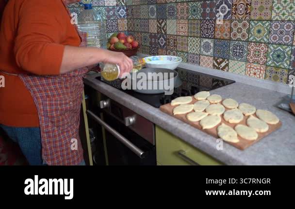 A woman pours sunflower oil into a frying pan to fry pies. Cooking ...
