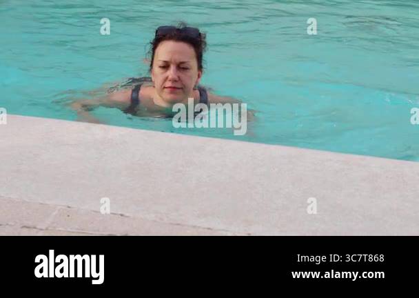 A woman enjoys a peaceful swim in a clear pool, focusing on her strokes ...