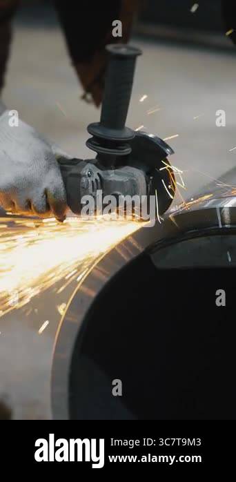 A worker at a metalworking factory processes metal. Sparks fly from a ...
