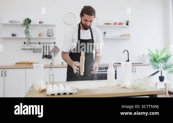 Adult male baker making dough in bright home kitchen environment with ...