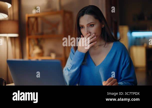 Concerned brunette reading email at laptop in dark home closeup. Desperate woman crying losing ...