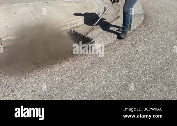 Person sweeping dust and sand off asphalt near curb with round brush on ...