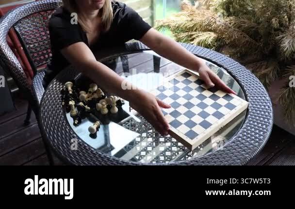 A woman sits on a terrace and plays chess on a glass table. The sun ...