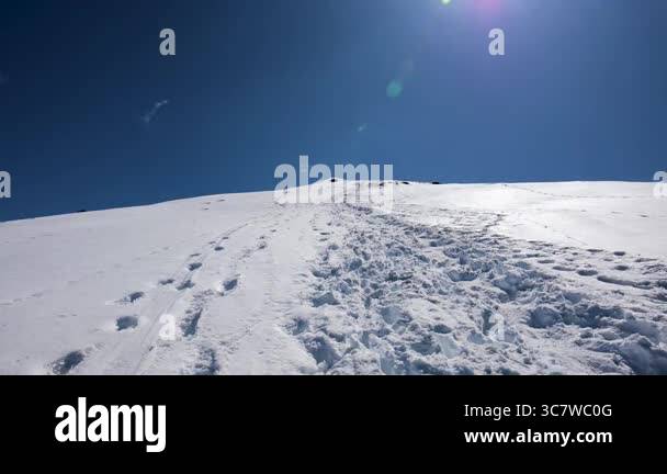 snowy trails leading to snowcap mountain summit with bright blue sky at ...