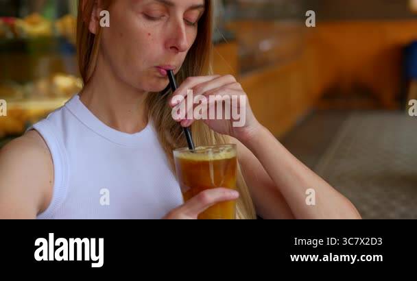 Woman stirs iced coffee with straw while relaxing in a modern cafe ...