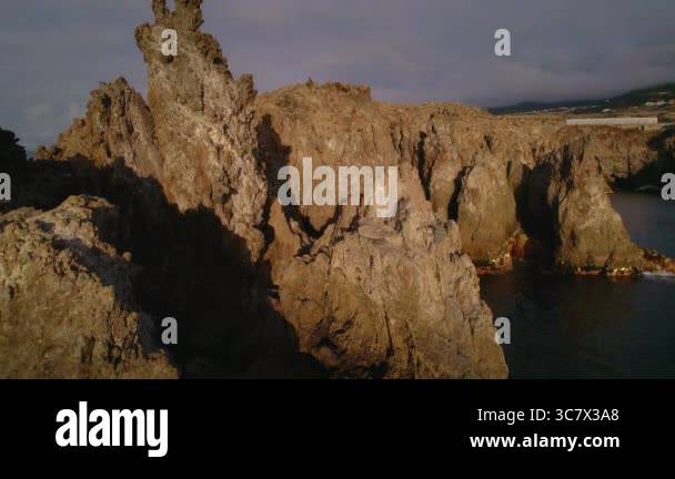 Sun casts long shadows over rugged coastal cliffs, with calm ocean ...