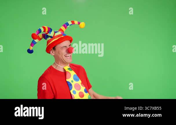 Clown wearing colorful jester hat and red nose laughs heartily against ...