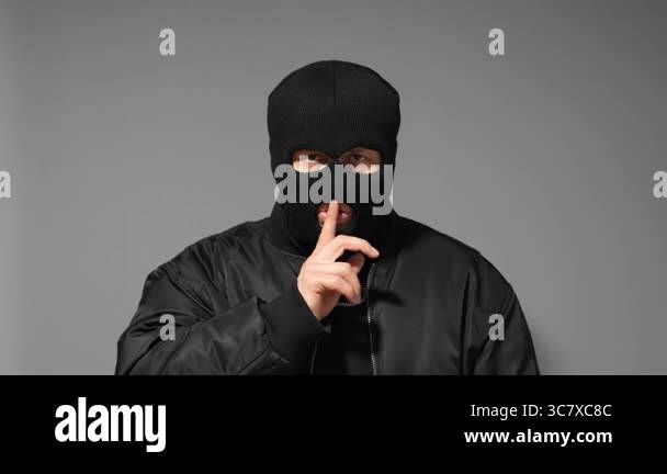 Criminal wearing balaclava showing silence sign with finger on lips ...