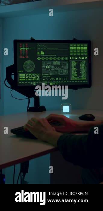 Male hacker with hood on his head in front of large computer monitors ...