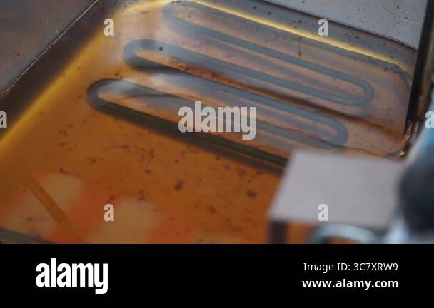 Close view of a heating element submerged in frying oil, showing wear ...
