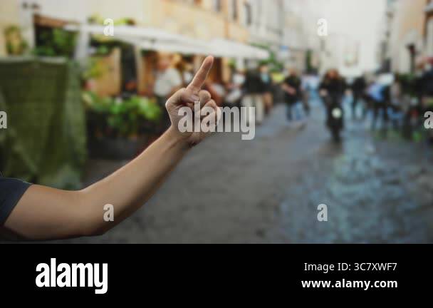 Man's hand with raised index finger gestures in a vibrant outdoor city ...
