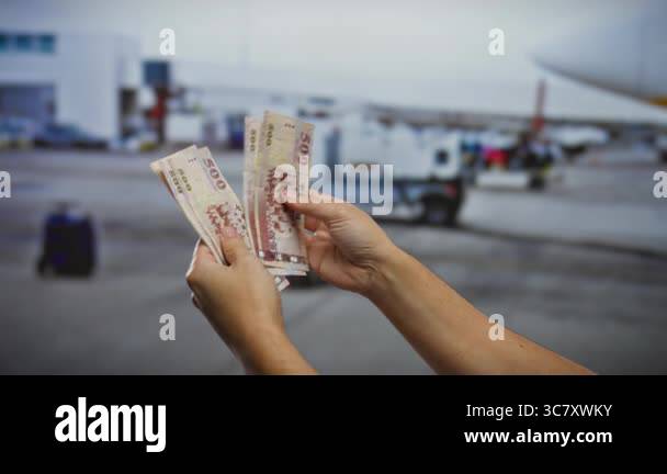 Hands holding taiwanese dollars at an airport with a plane in the ...
