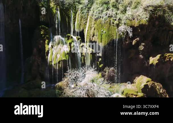 Pristine waterfalls cascading down moss-covered rocky cliff, revealing ...