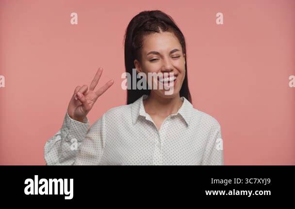 Cheerful young woman in a polka-dot shirt winks and flashes a peace ...
