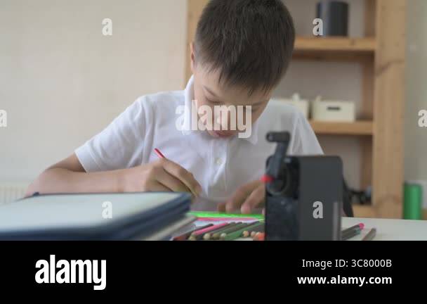 A homeschooled schoolboy does his homework. The boy sits at the table ...
