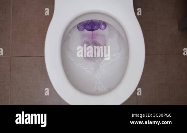 Close-up top shot captures a white toilet bowl during a flush cycle ...