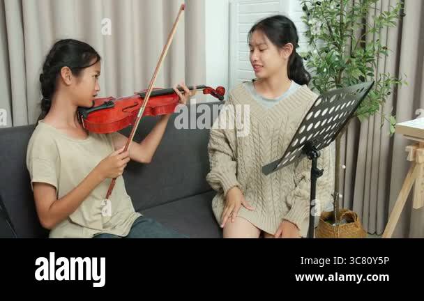 Young girl and her older sister enjoy playing violin at home during ...