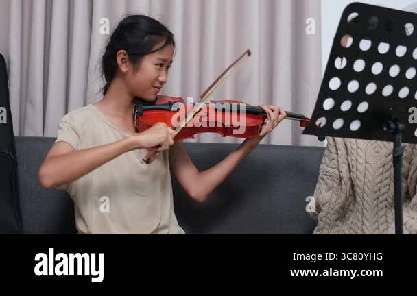 Young girl and her older sister enjoy playing violin at home during ...