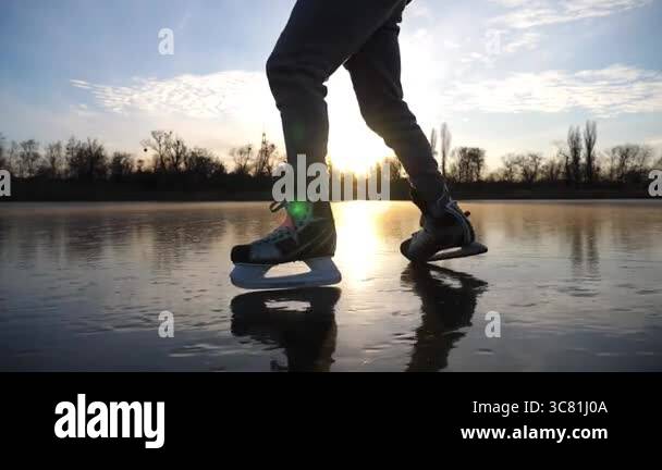 Male feet shod in figure skates sliding on ice rink at sunset. Legs of ...