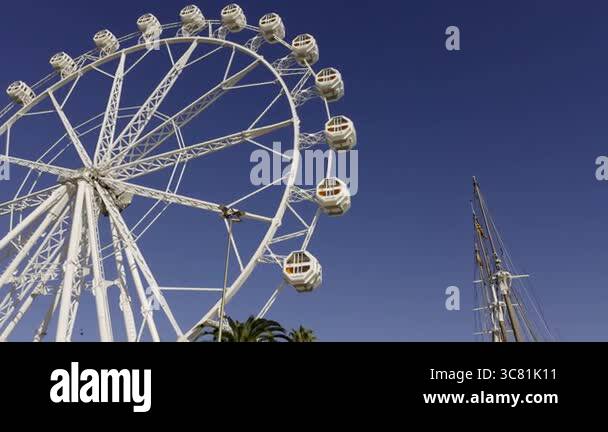 Ferris wheel rotating against a clear blue sky, next to a sailing ship ...