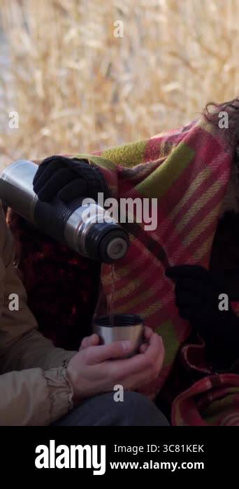Content family couple enjoys drinking tea together while strolling outdoors in nature, sharing ...