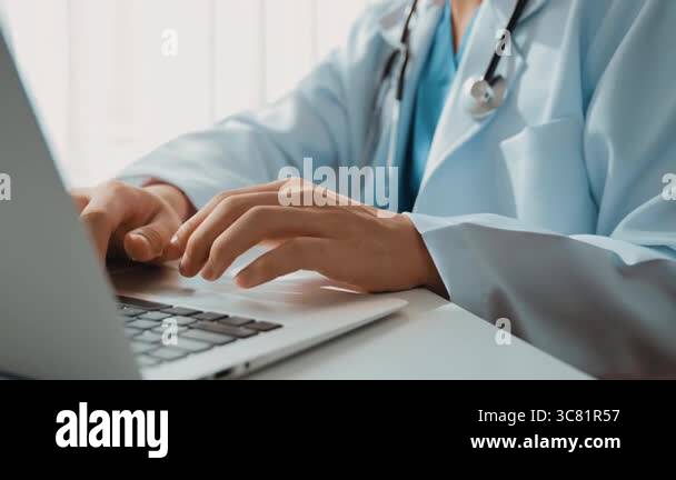 Doctor at hospital sit at his desk working on laptop diagnosing patient ...