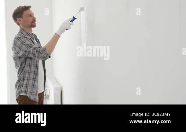 Professional painter rolling white paint on interior wall, carefully ...