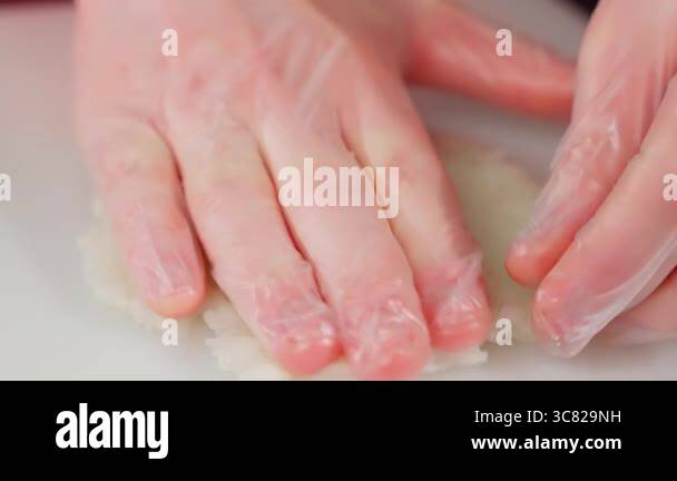 Chef pressing sticky sushi rice on a white surface with gloved hands ...