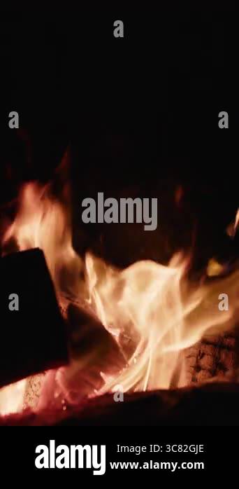 A bonfire burns brightly in the darkness, with flame particles drifting ...