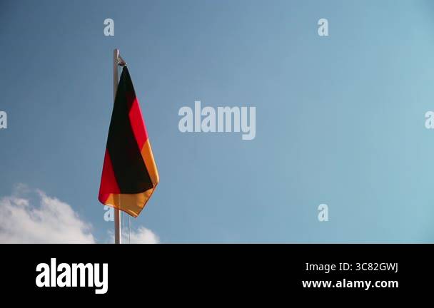 Hoisting a textile flag of Germany on a flagpole in front of blue sky ...