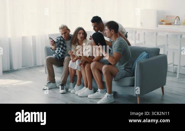 A diverse group of friends sits closely together on a cozy couch ...