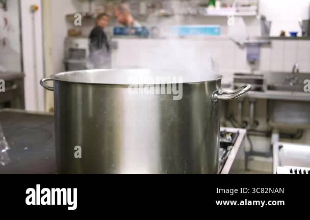 Steam rising from a boiling pot in a busy restaurant kitchen setting ...