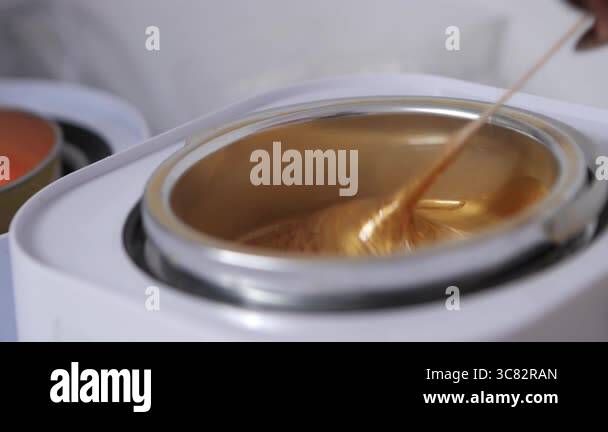 The hand of the depilatory master mixes the golden wax mixture melted ...