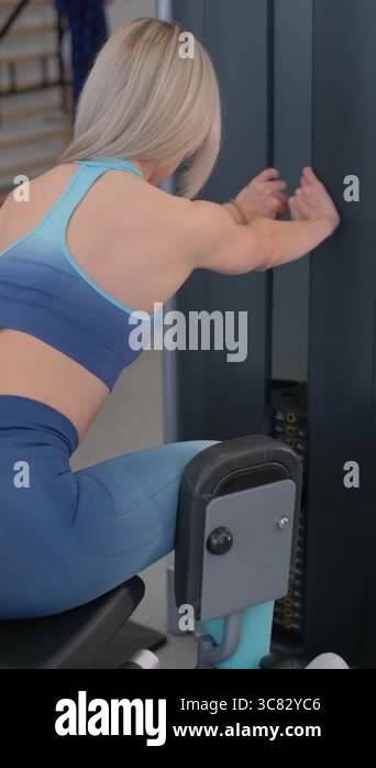 A fit blonde woman in a sleek fitness outfit performs leg exercises on ...